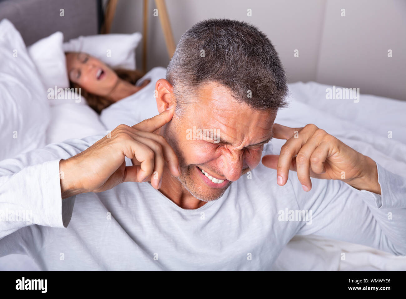 Angry Mature Man Plugging Ear With Finger While Sitting Near Snoring ...