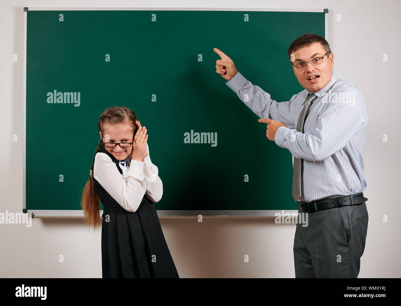 angry teacher shout to schoolgirl, posing at blackboard background ...