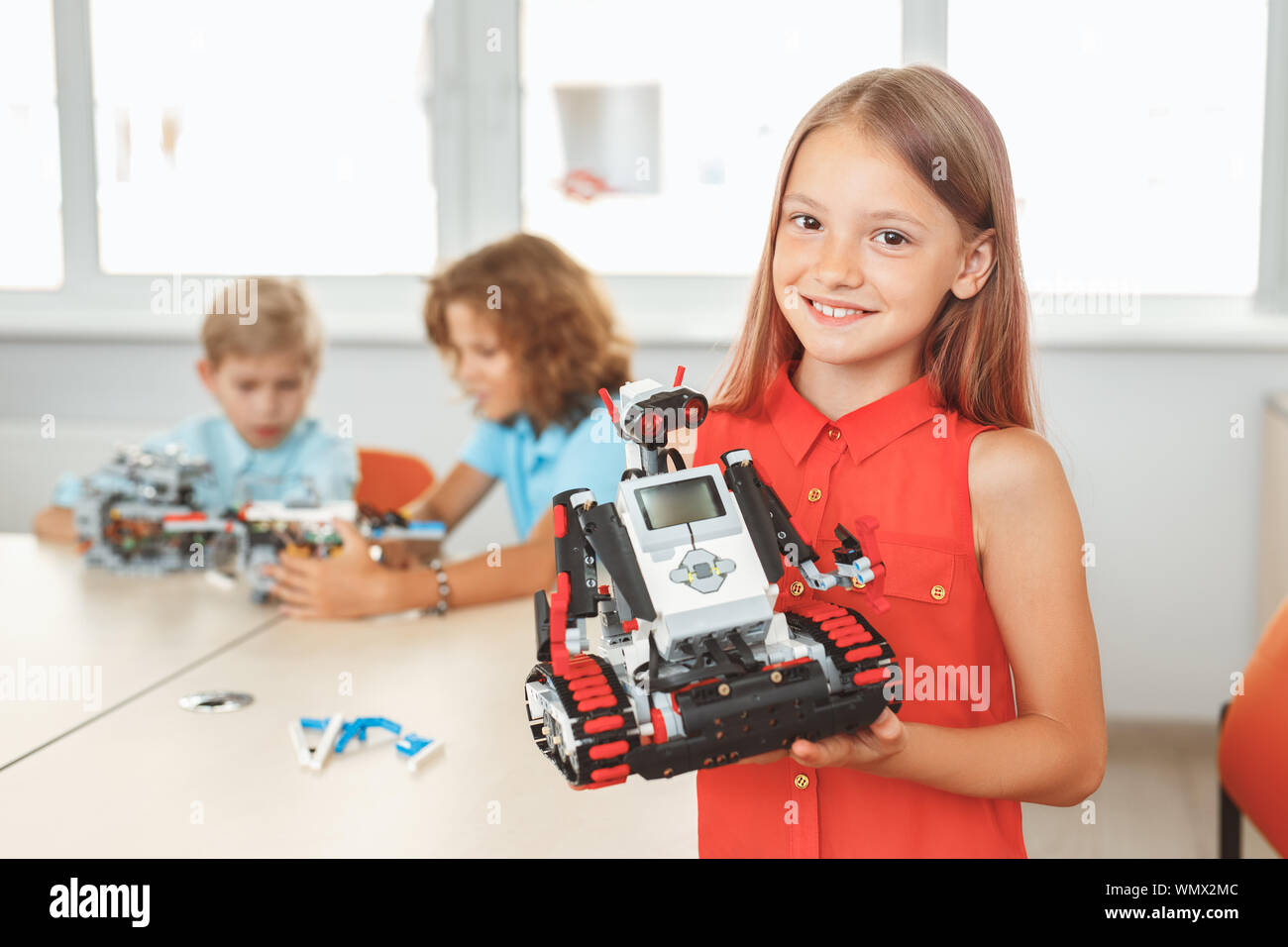 Children having robotics class sitting at table studying while girl ...