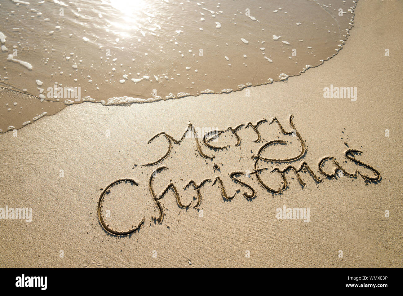 Merry Christmas message handwritten in smooth sand with an oncoming ...