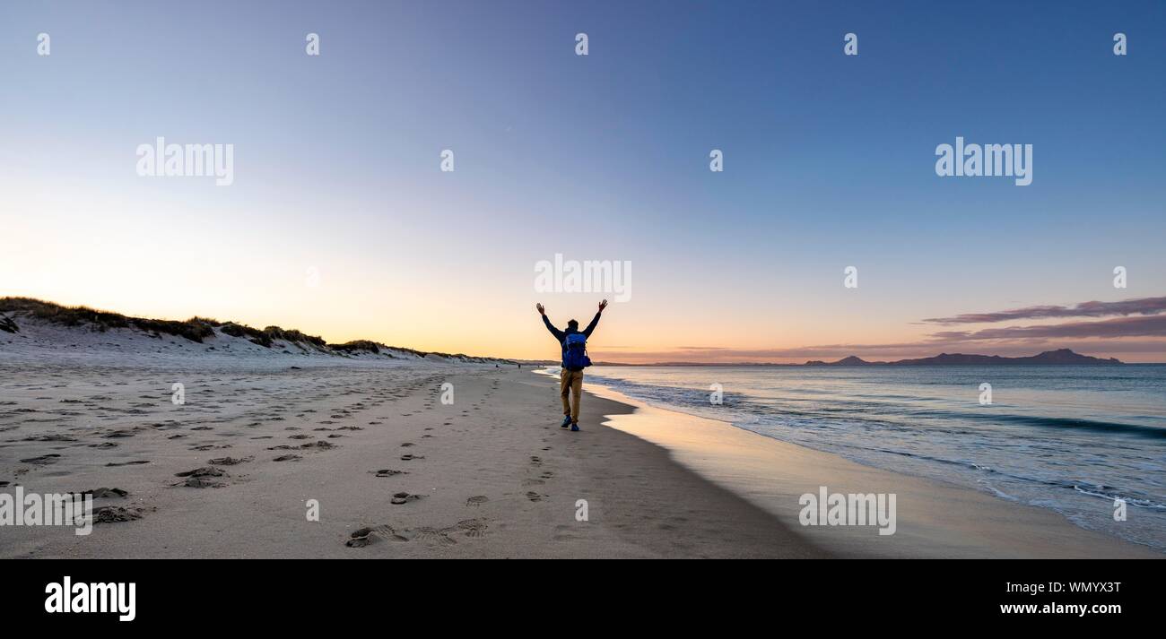 Young man walks on the beach and stretches his arms into the air, beach ...