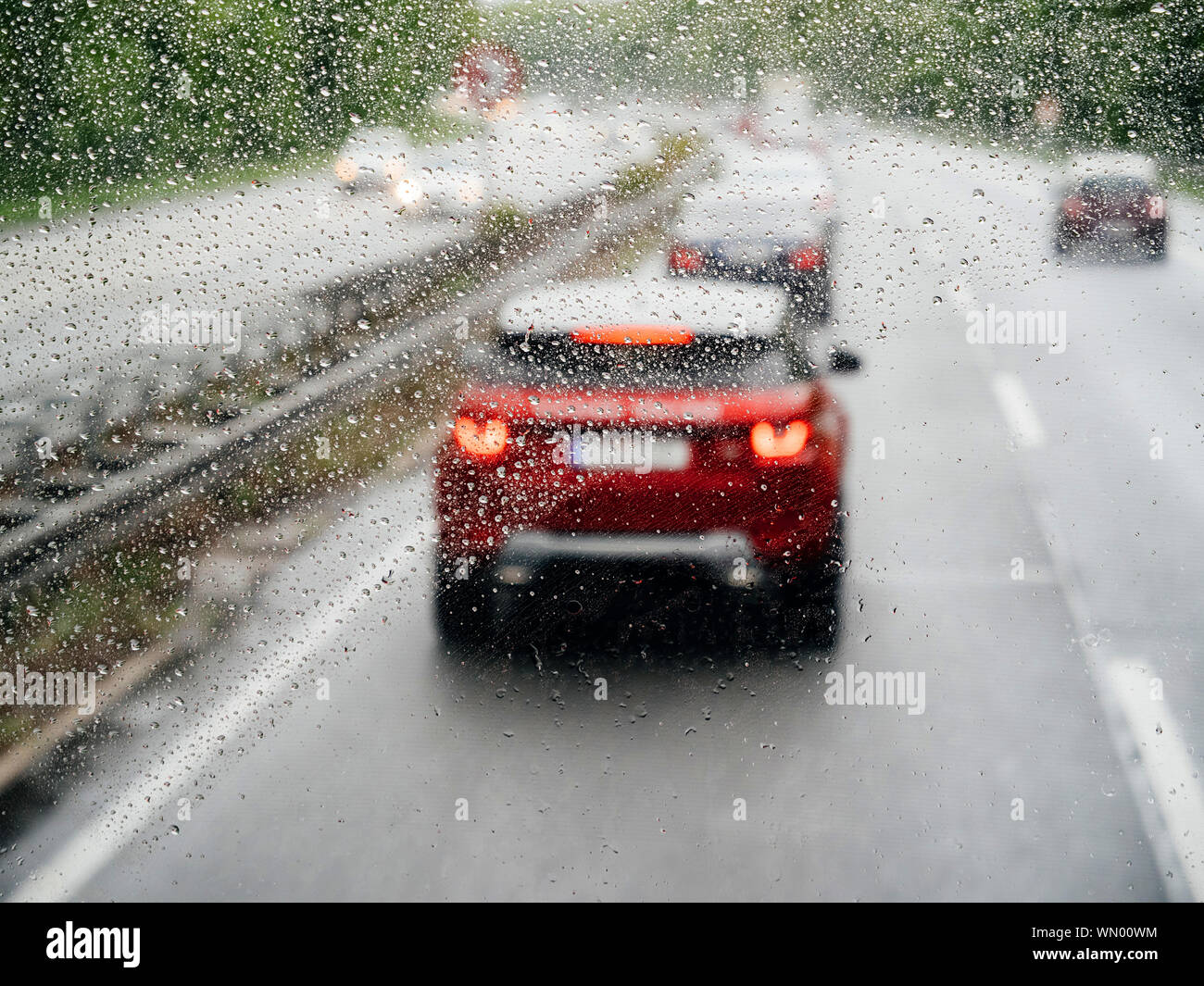 Elevated view over the front driving red car through the covered with raindrops windshield of ...