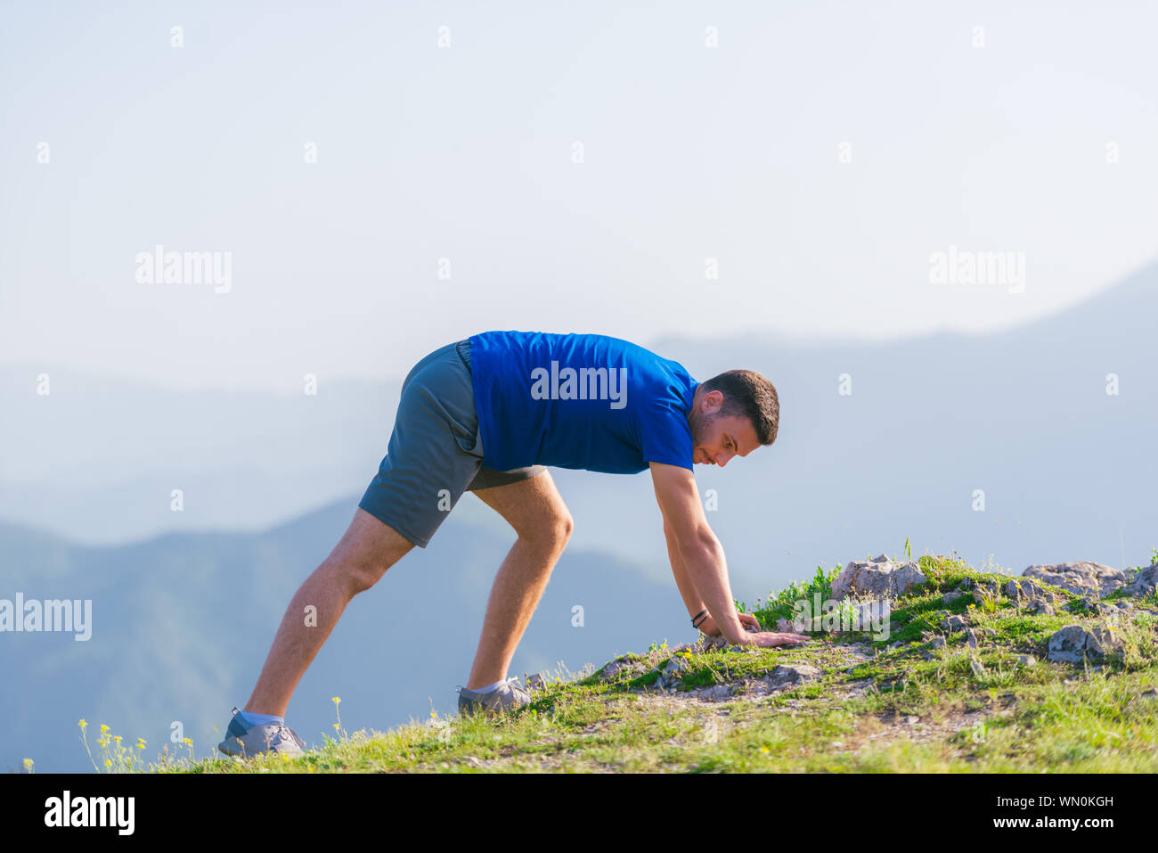 A young fit male athlete is doing push-ups outdoors on a cliff while ...