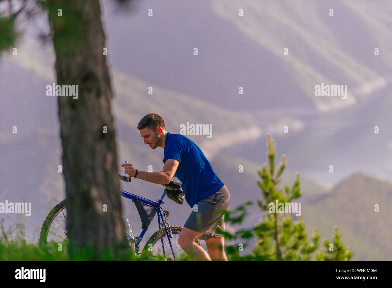 Tired cyclist is wiping his sweat off his face while pushing his ...