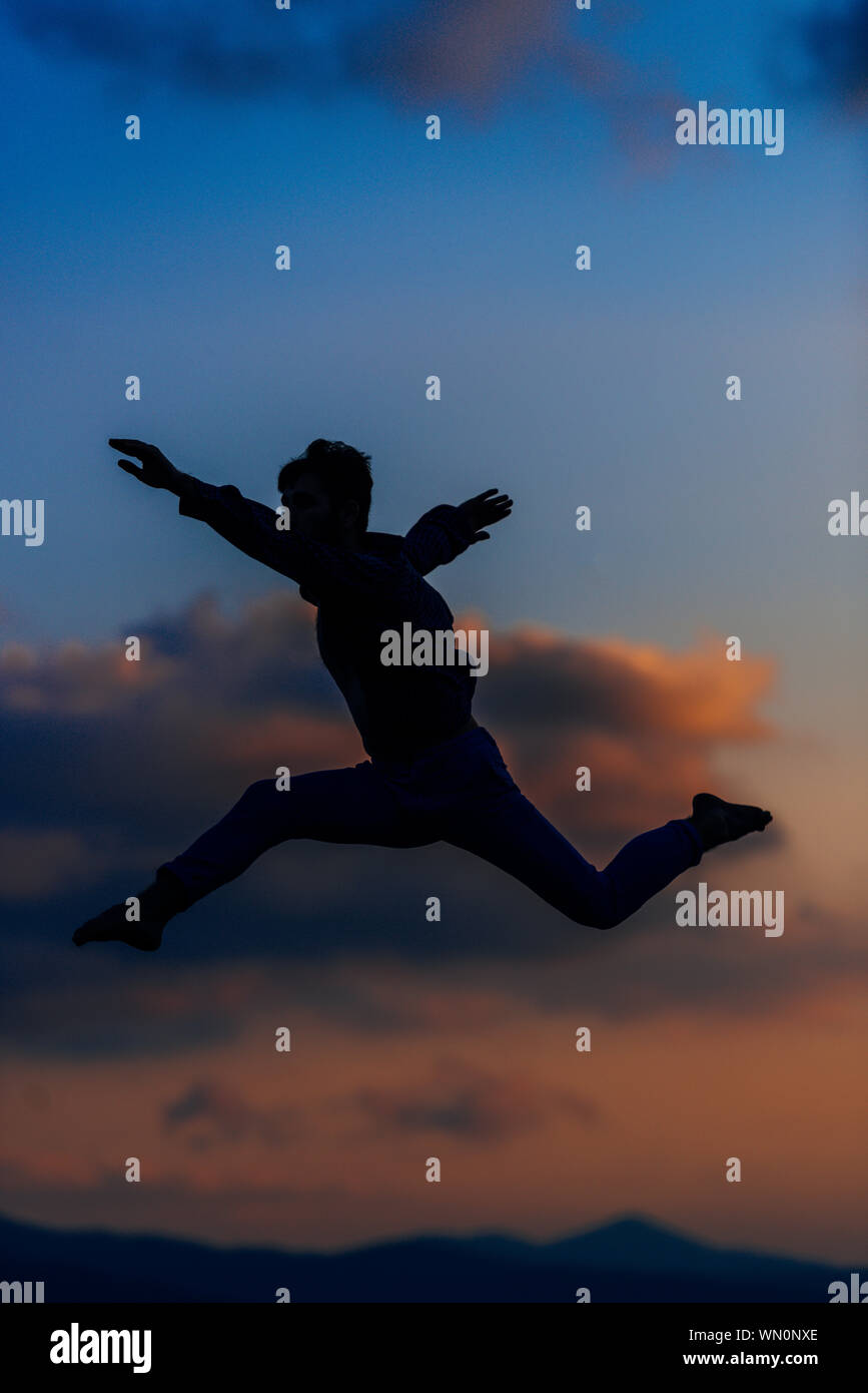 Young ballet dancer in leaping on air against blue sky with clouds ...