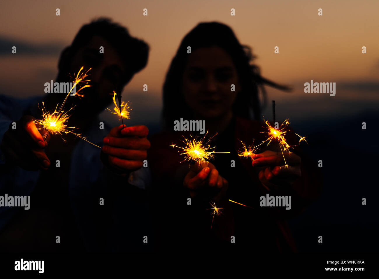 Lighting sparklers burn in male and female hands over dark night sunset ...