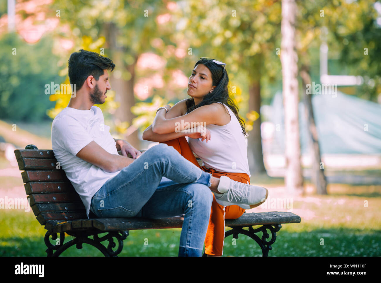 Happy casual couple talking looking each other sitting in a park with a ...