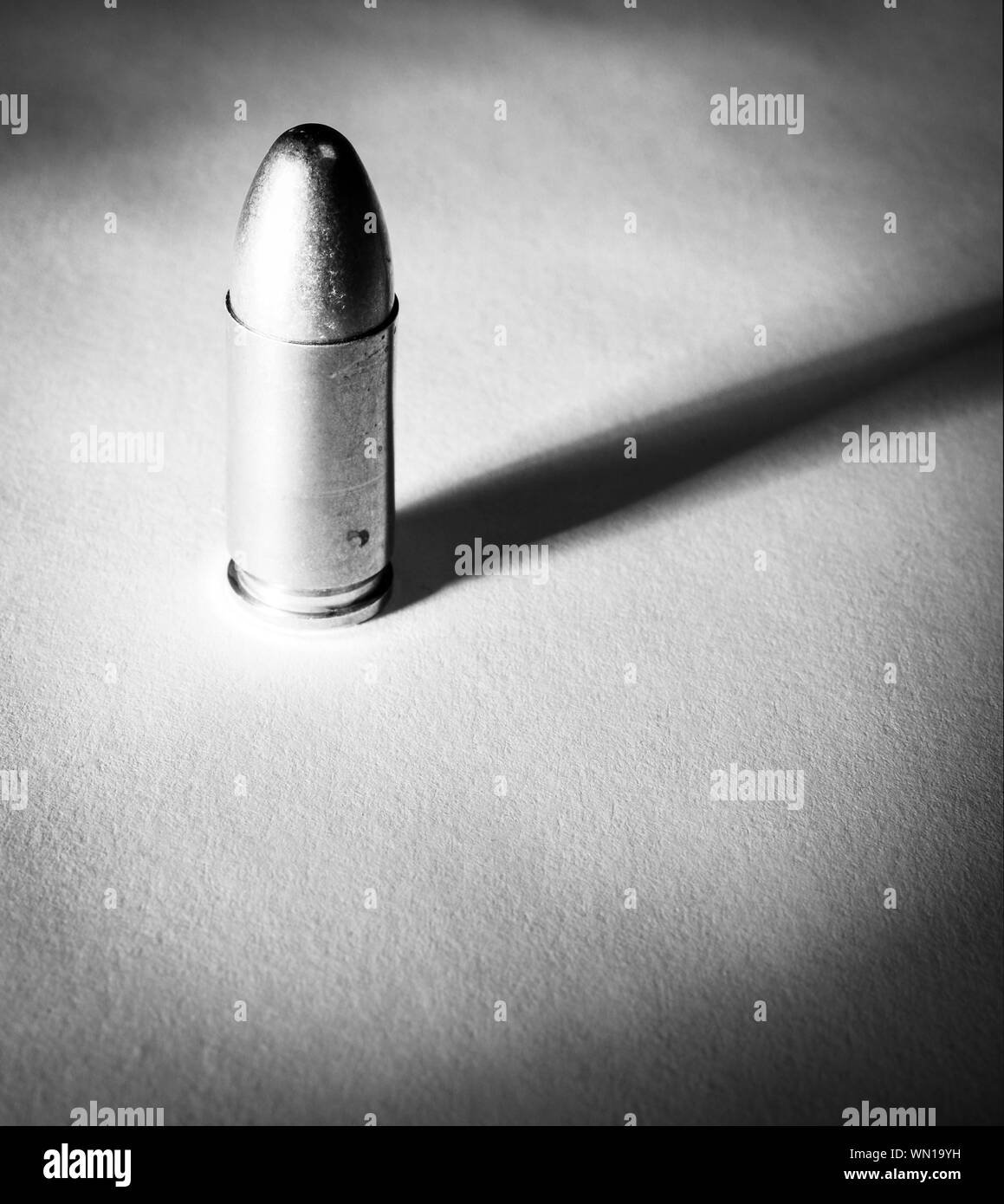 A single standing 9mm bullet with dramatic side light and shadows in ...