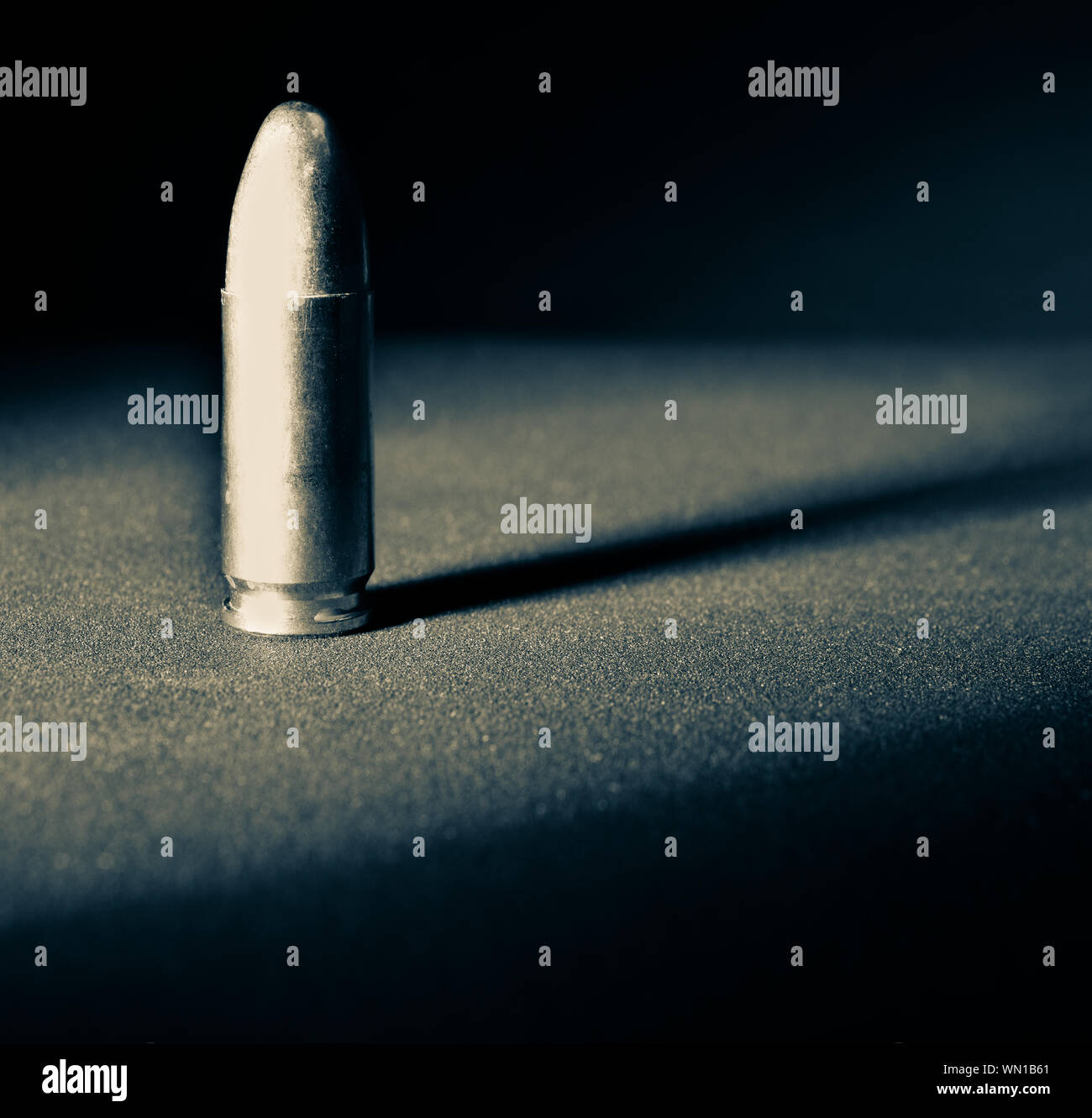 A single standing 9mm bullet with dramatic side light and shadows in ...