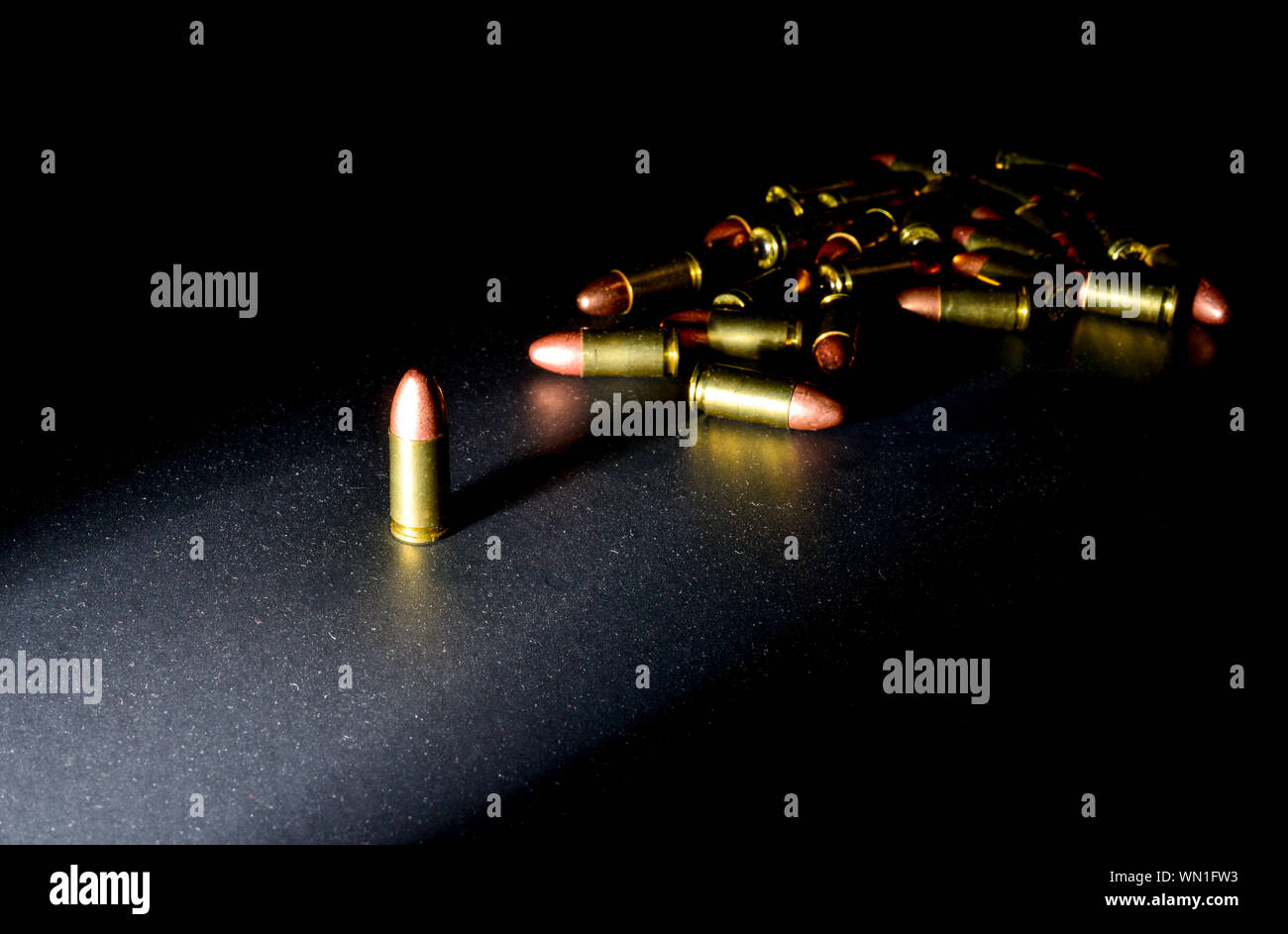 A single 9mm bullet stands alone with strong side light creating ...