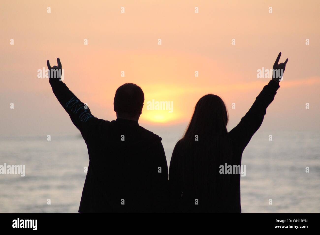 Silhouette of a couple signing devil horns with a blurred background ...