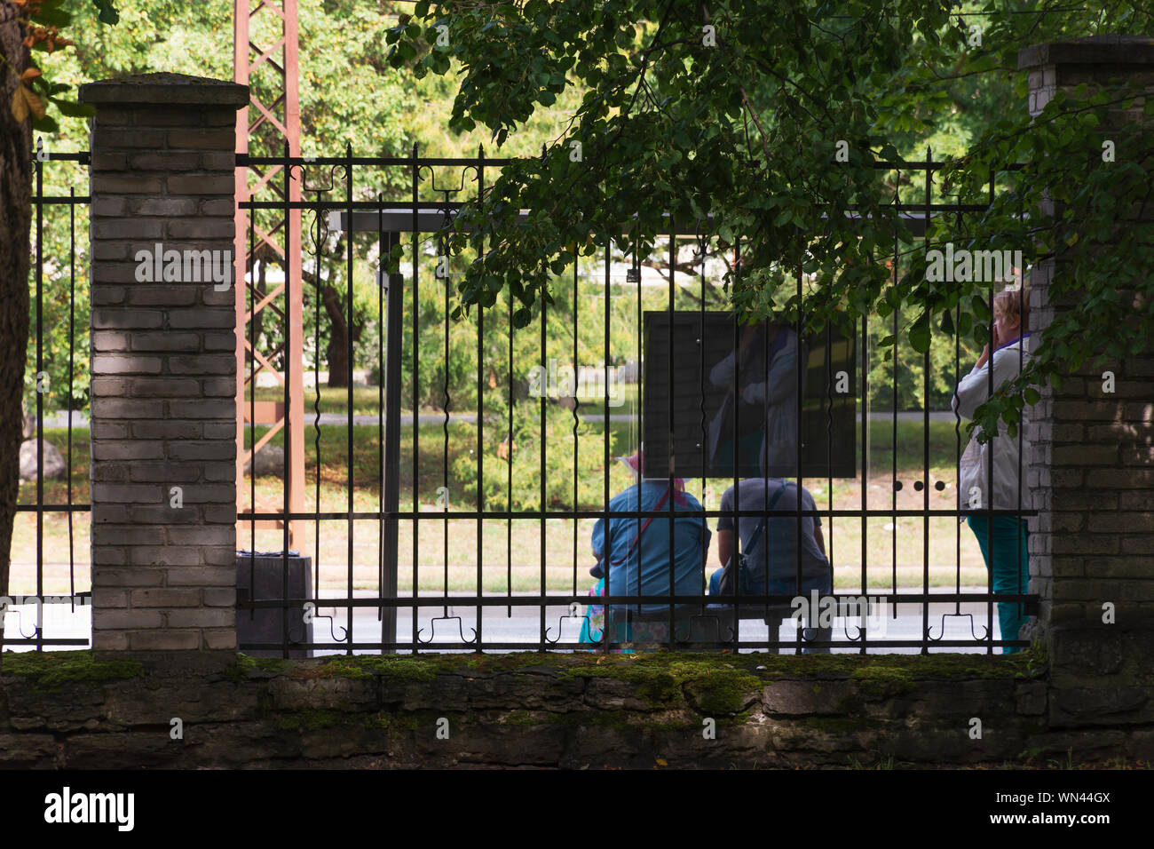 Two women sitting on a bench and one standing outside of Kopli Cemetery ...