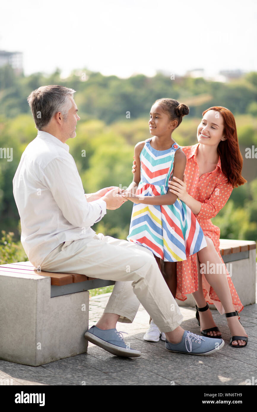 Dark-skinned girl getting acquainted with foster parents Stock Photo ...