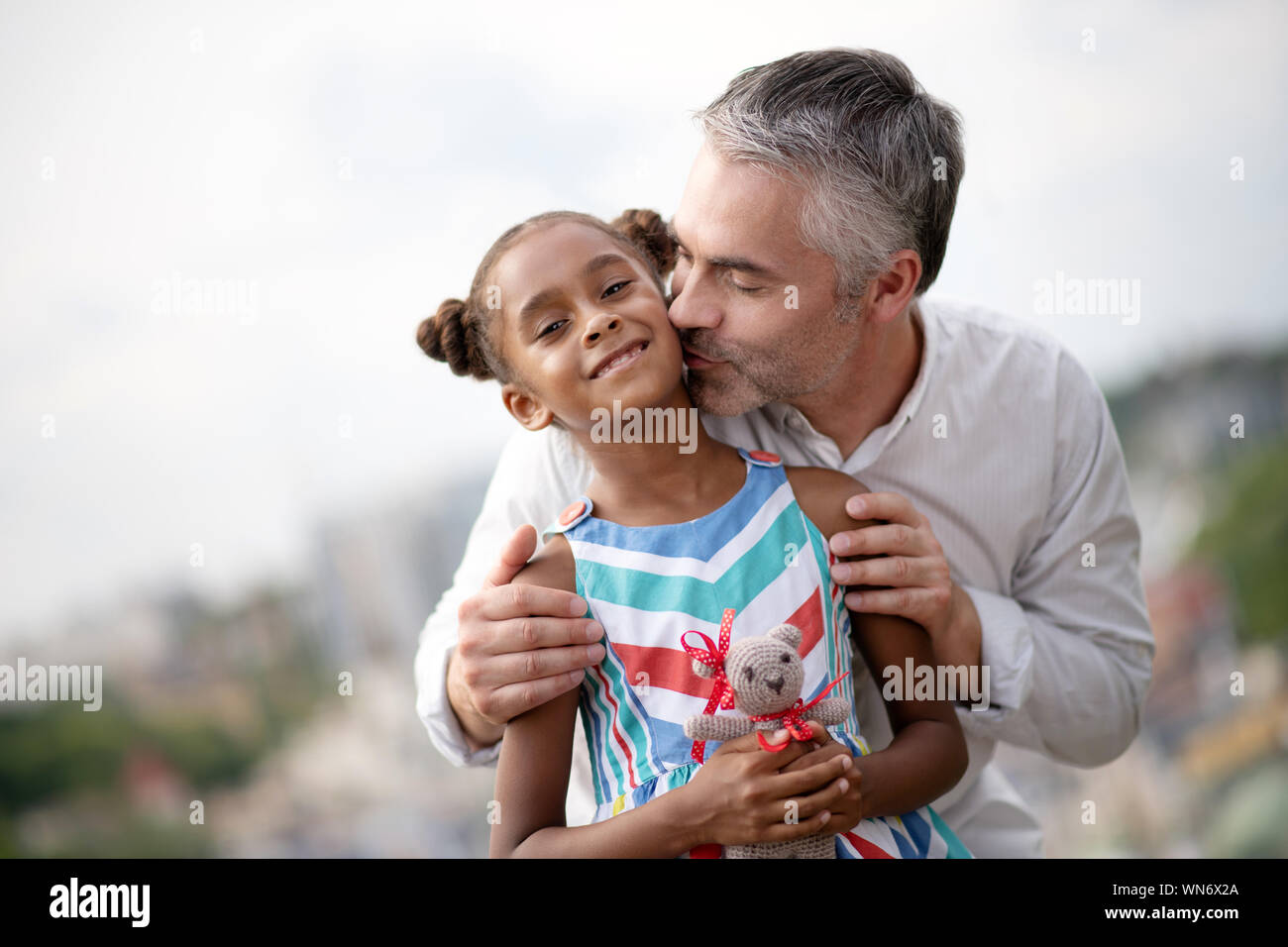 Grey-haired foster father kissing his cute dark-skinned daughter Stock ...