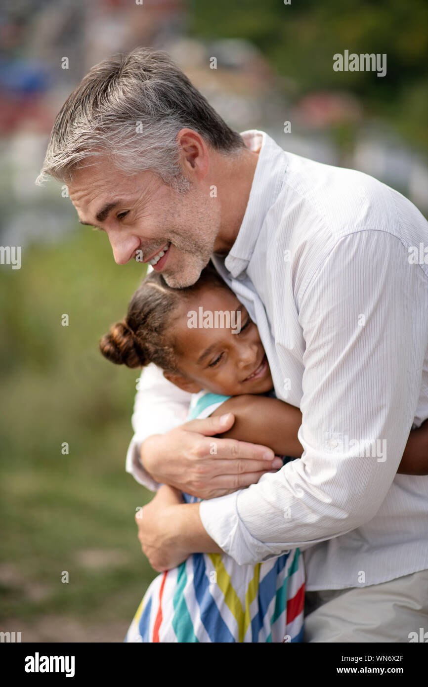 Beaming loving father hugging his cute dark-skinned daughter Stock Photo - Alamy