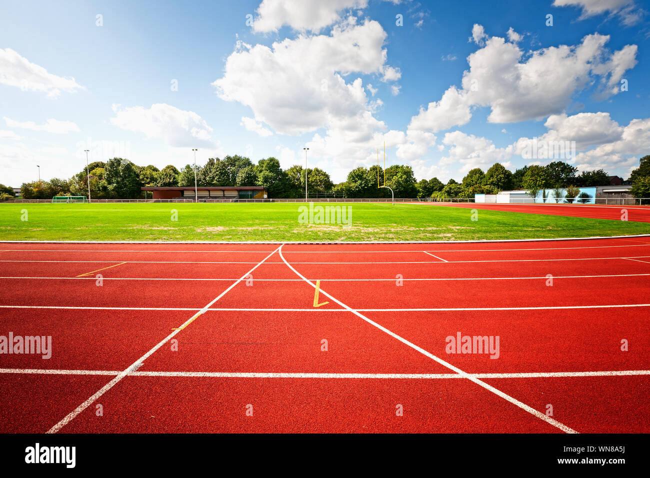 Red running track in stadium over blue sky with clouds in summertime ...