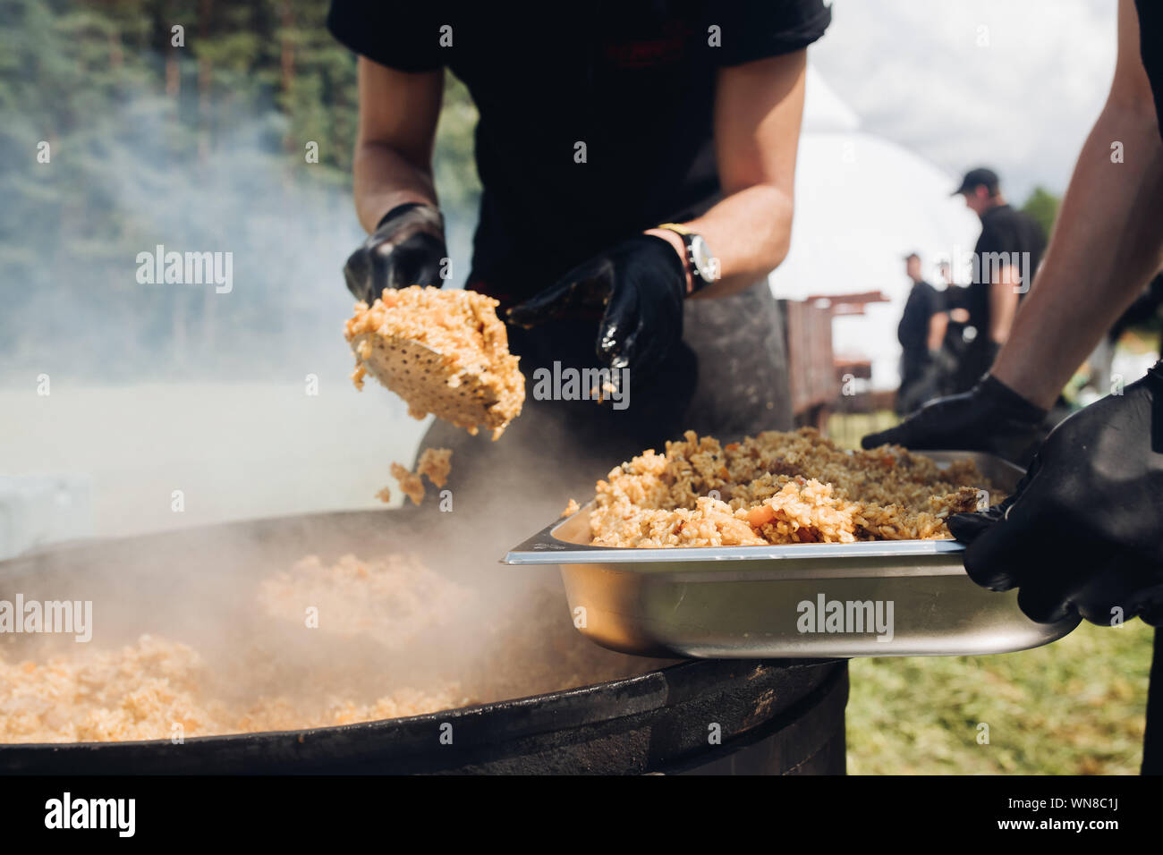 Men putting pilaf from cauldron into container Stock Photo - Alamy