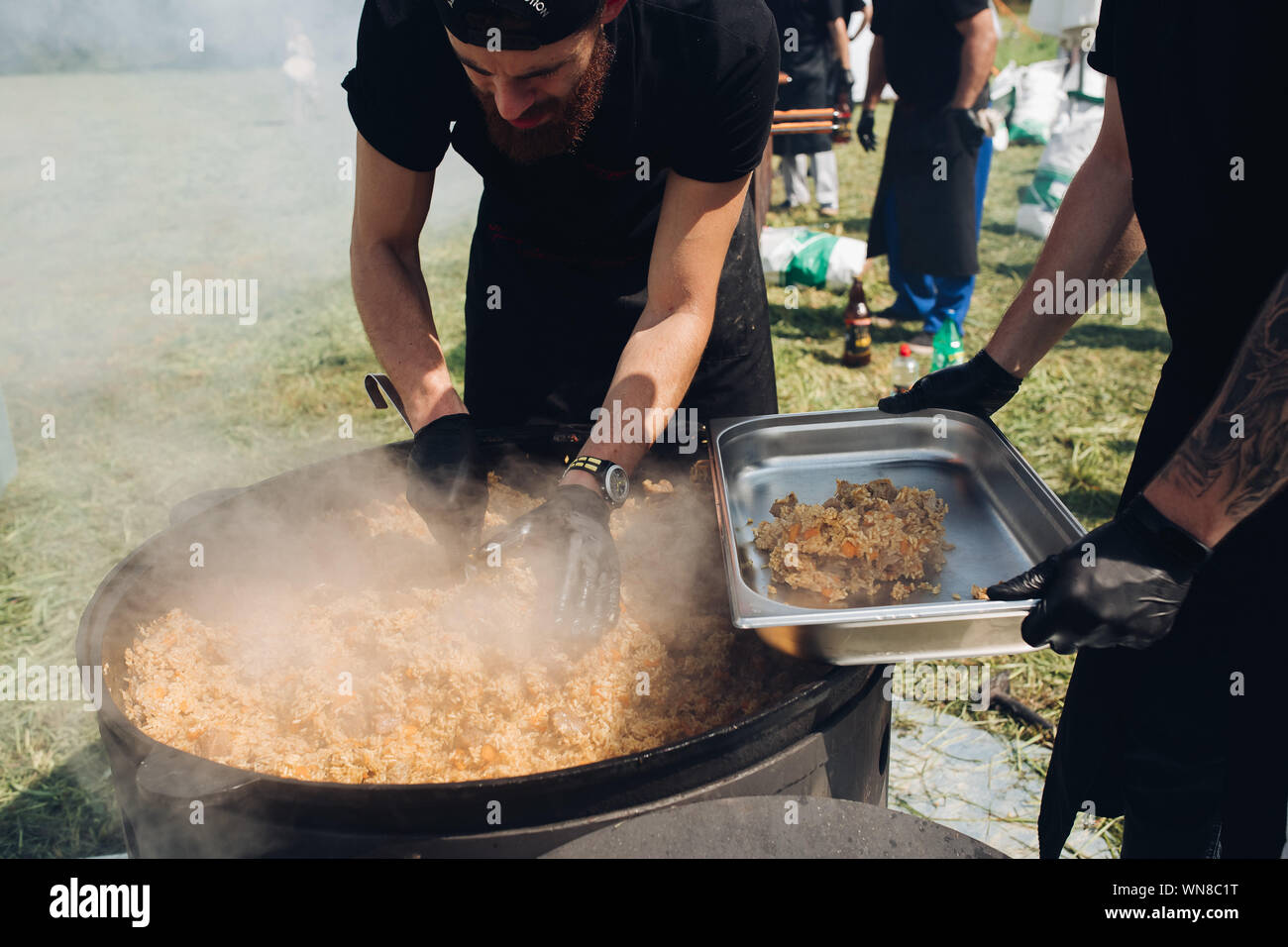 Men putting pilaf from cauldron into container Stock Photo - Alamy