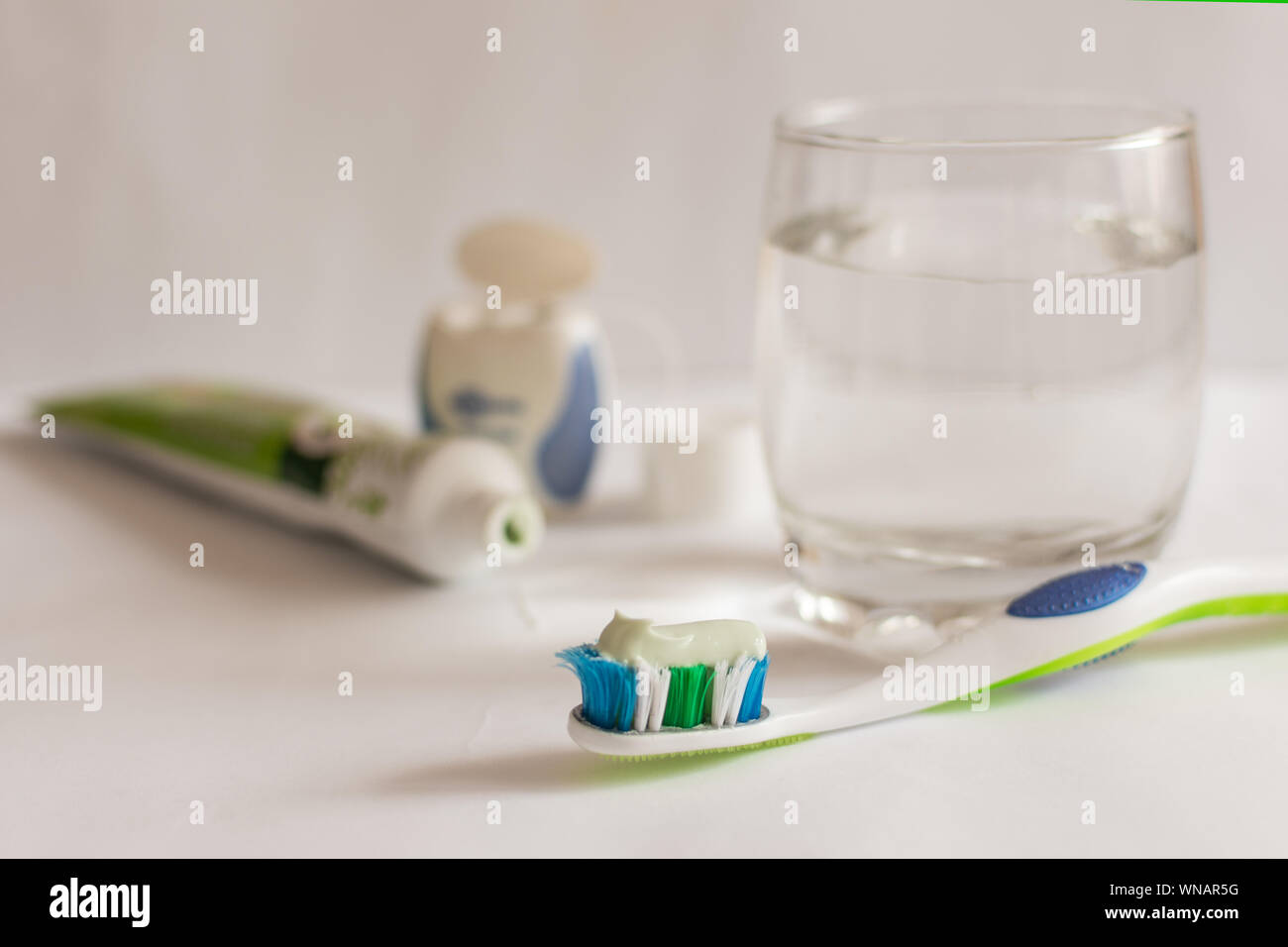 Green toothbrush with toothpaste and a glass of water on white ...