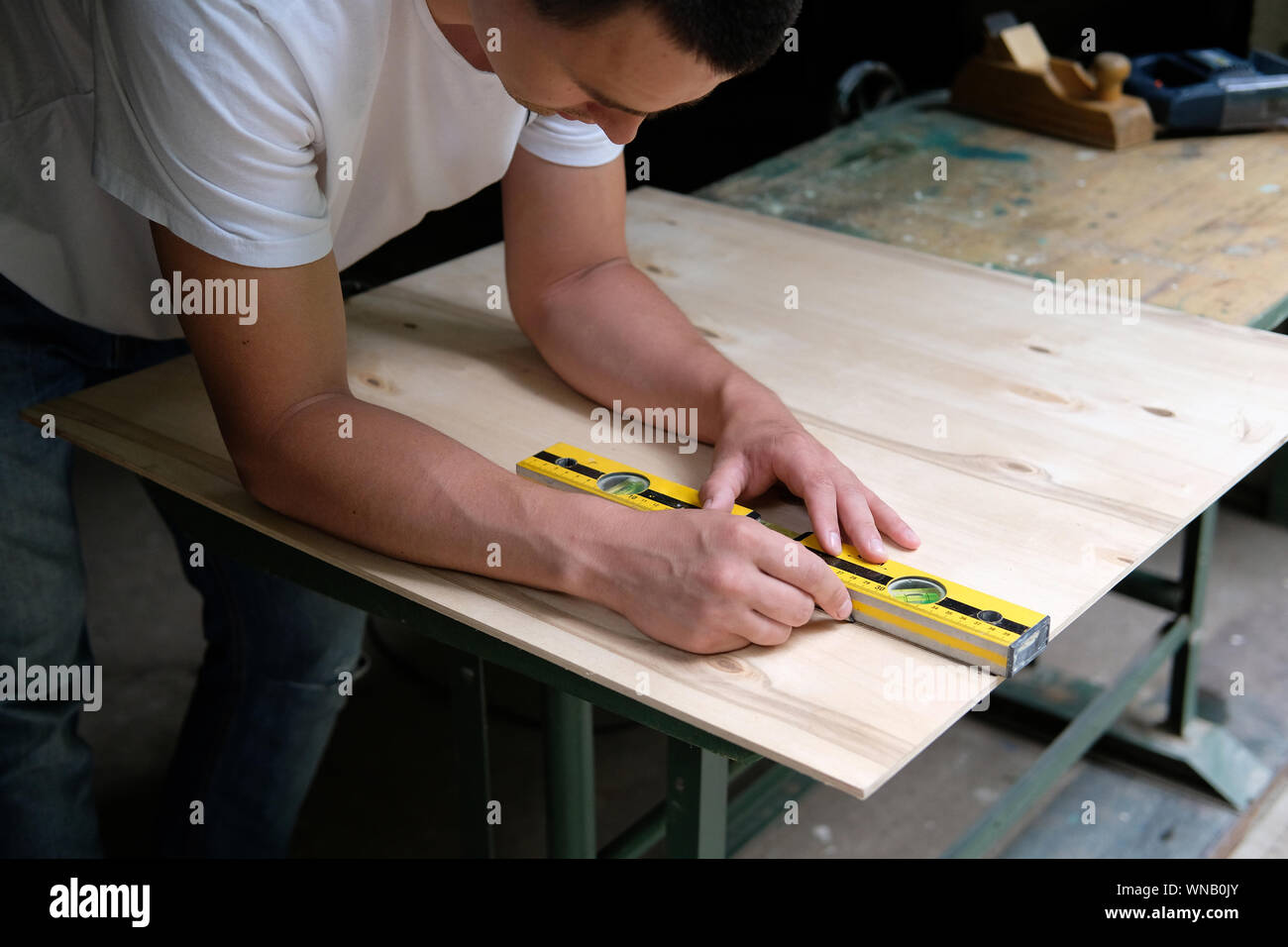 Carpenter marking straight line on plywood sheet using spirit level in ...