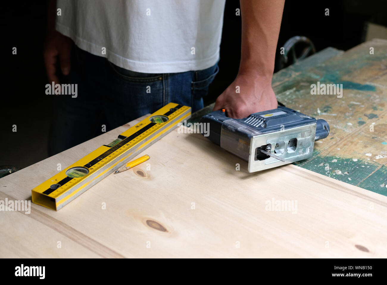 Hands of human holding electric jigsaw lying on workbench with spirit ...