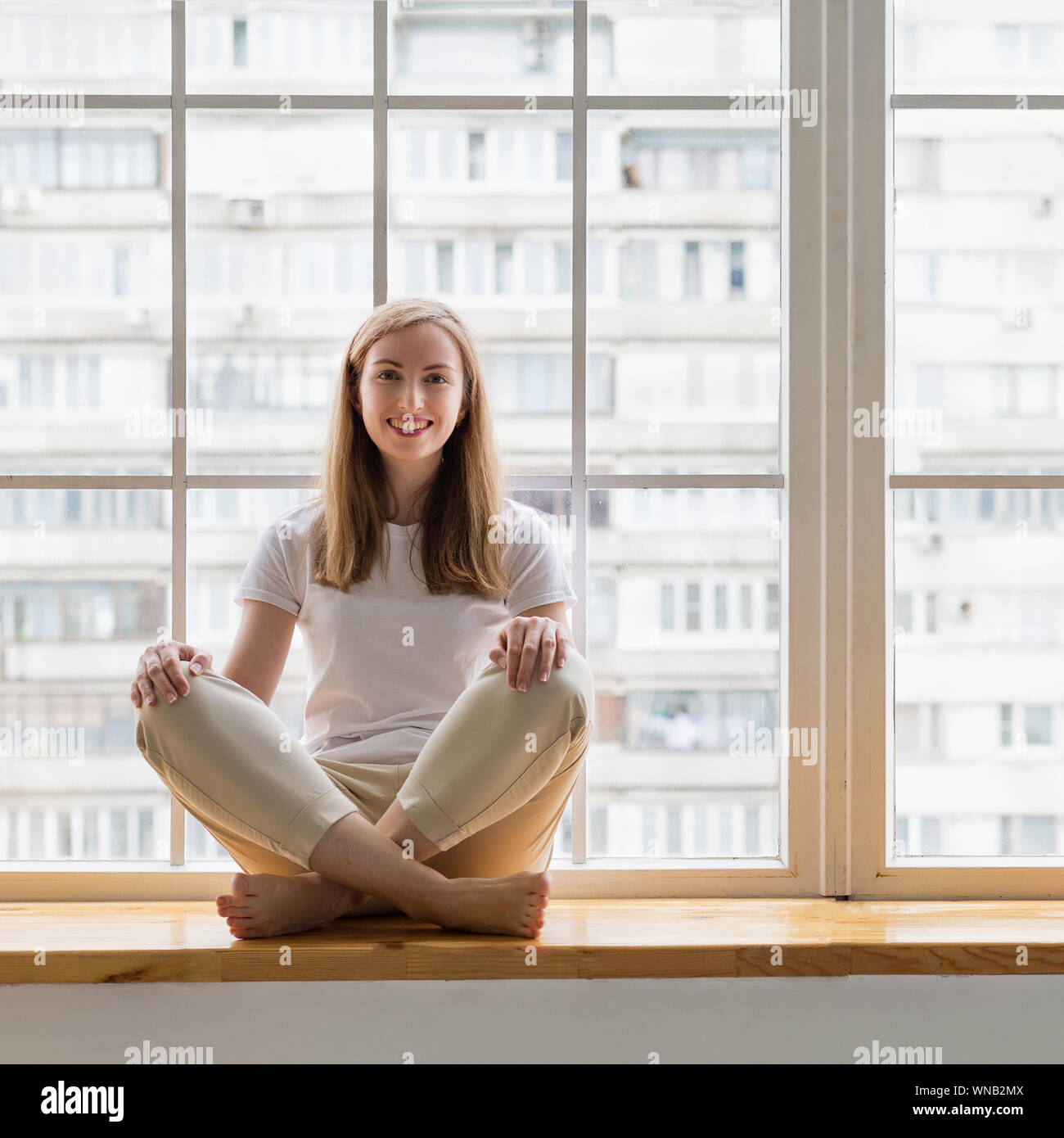 Young smiling woman sitting on window sill Stock Photo - Alamy