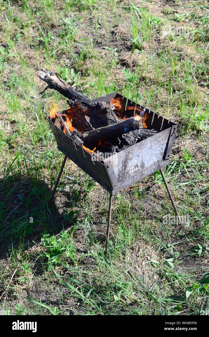 Firewood burns inside the grill in forest field outdoors in warm sunny ...