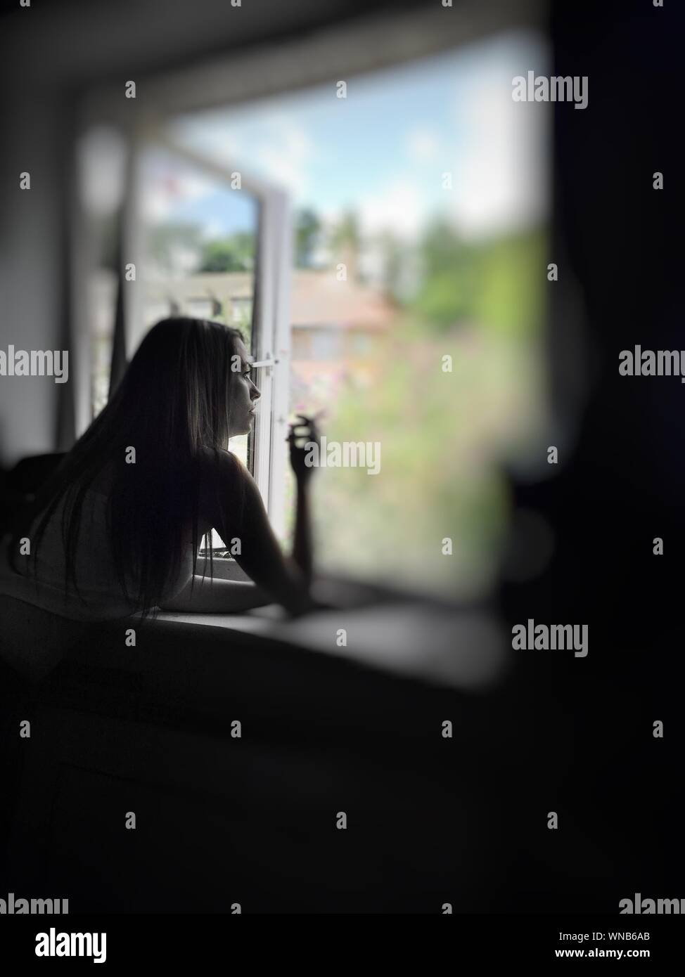 Young Woman Smoking While Looking Through Window At Home Stock Photo ...