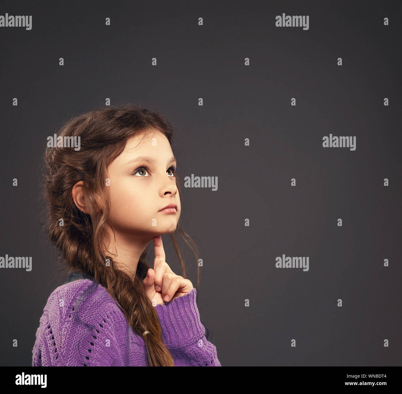 Thinking sad dreamy serious cute kid girl looking up on grey studio ...