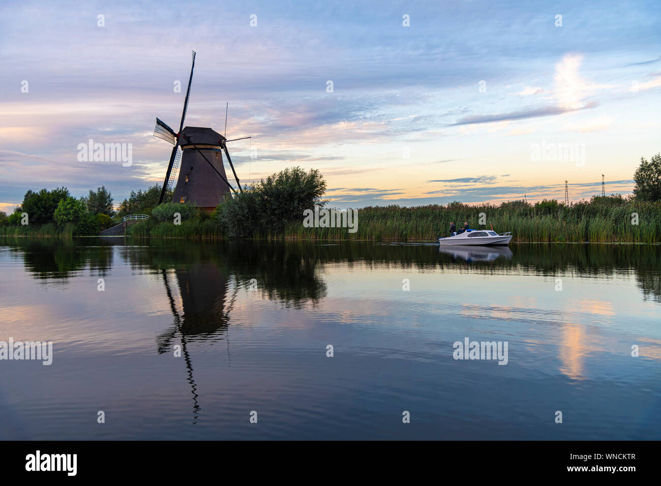 Dutch windmill laying along the canal with wild grass blown by strong ...