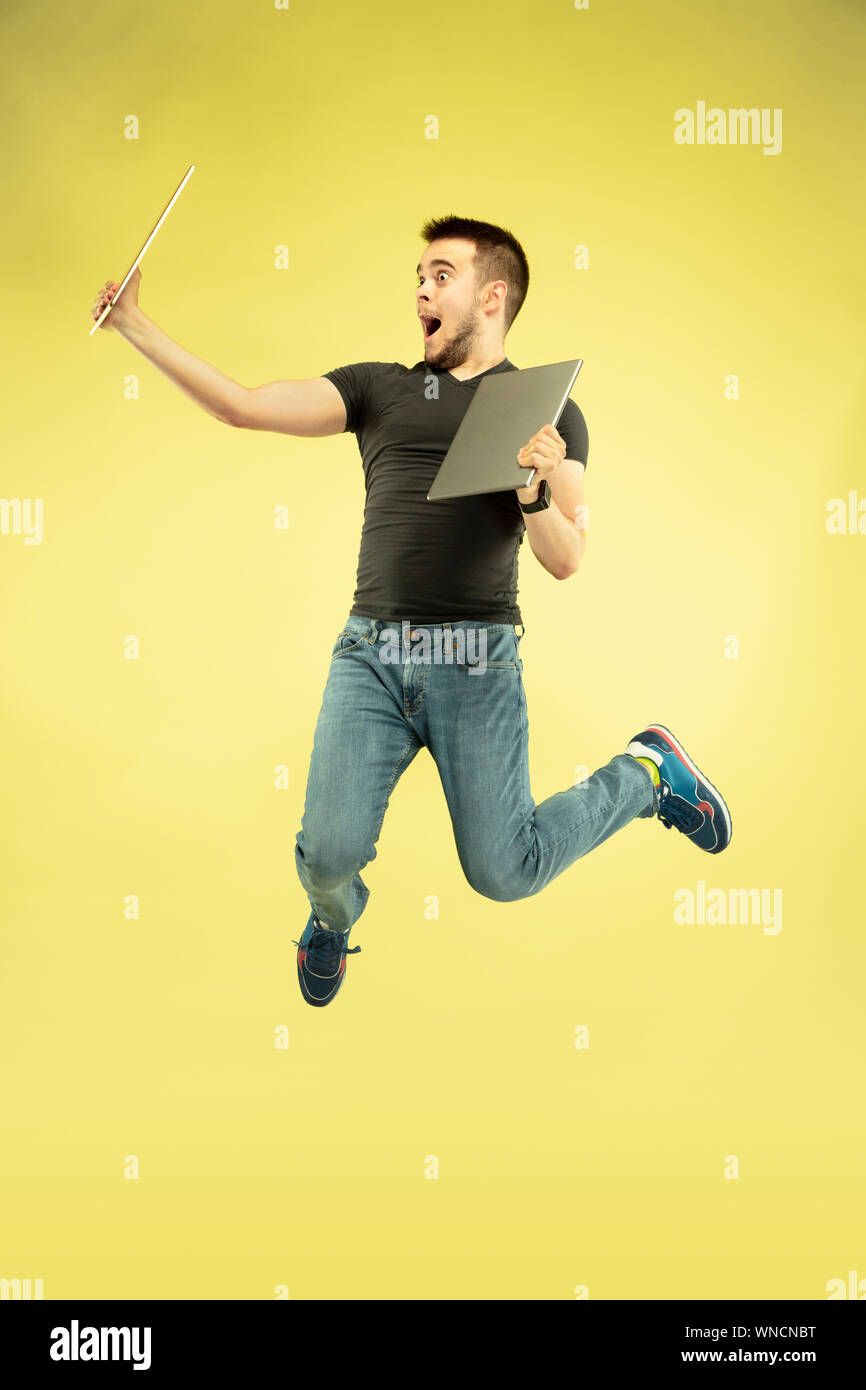 Weightless. Full length portrait of happy jumping man with gadgets ...