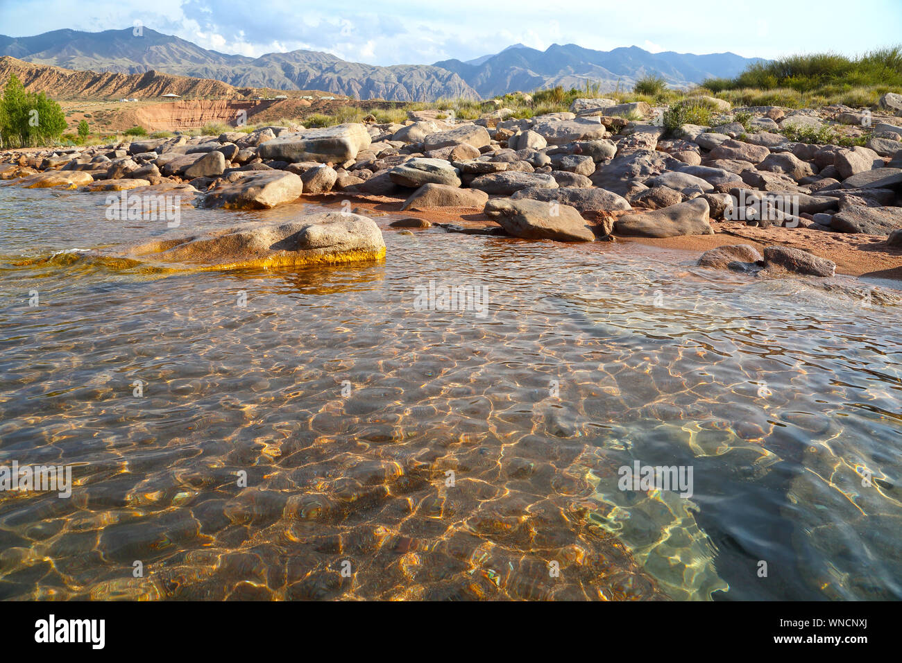 The shore of a mountain lake with clear clear water. Sunny day, ripples ...