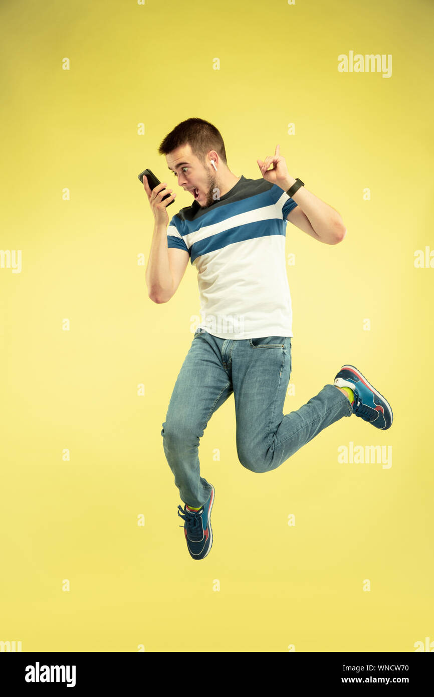 Full length portrait of happy jumping man with gadgets on yellow ...