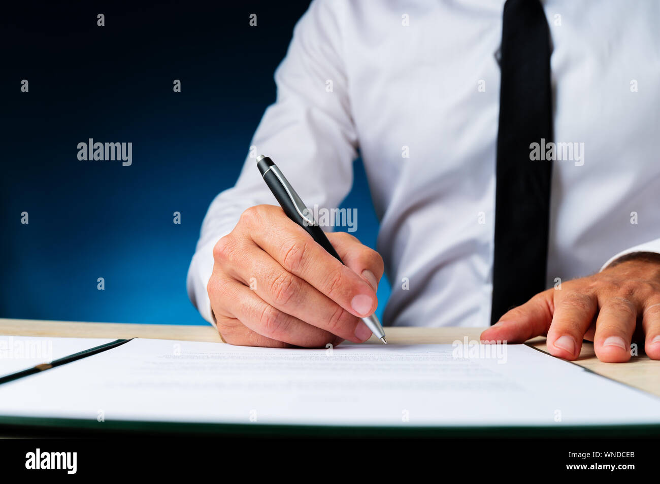 Business manager signing a document in a folder on his desk. Over dark ...