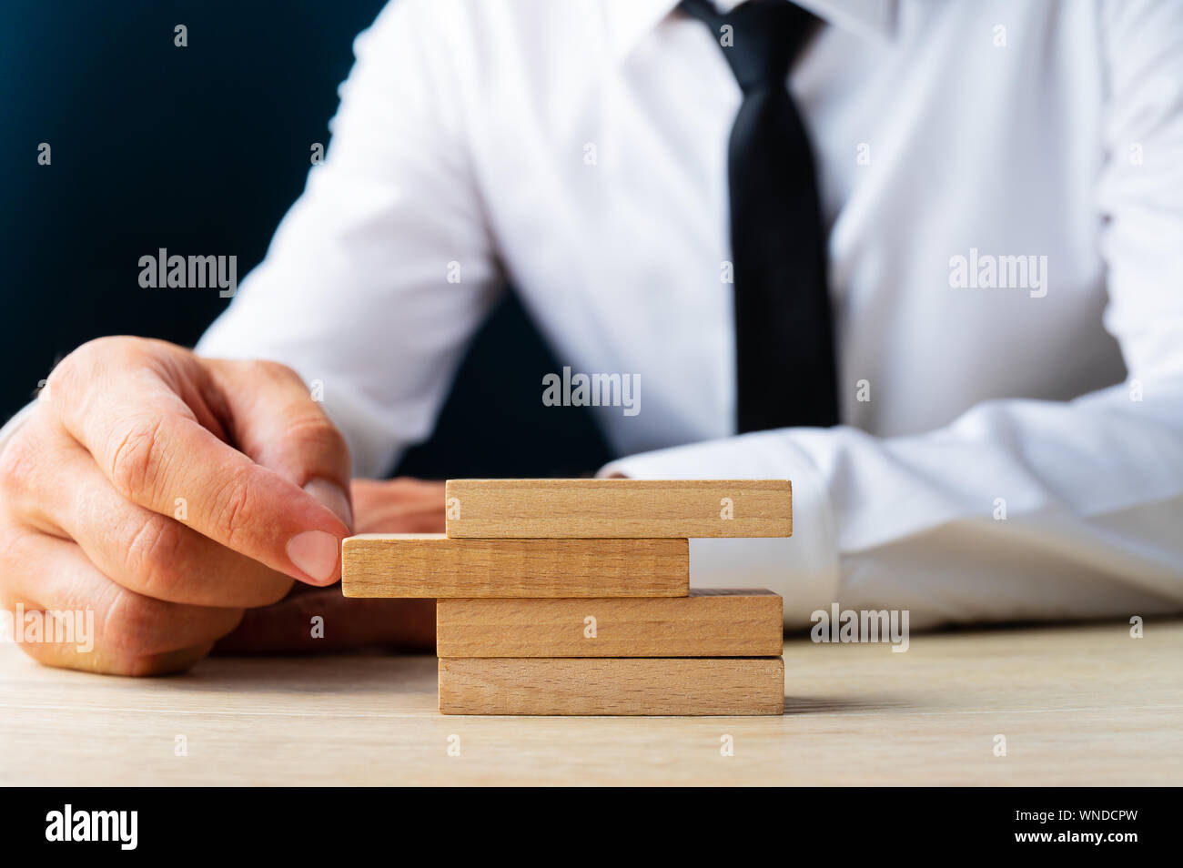 Businessman sitting at his desk pushing a peg in to a stack of them in ...
