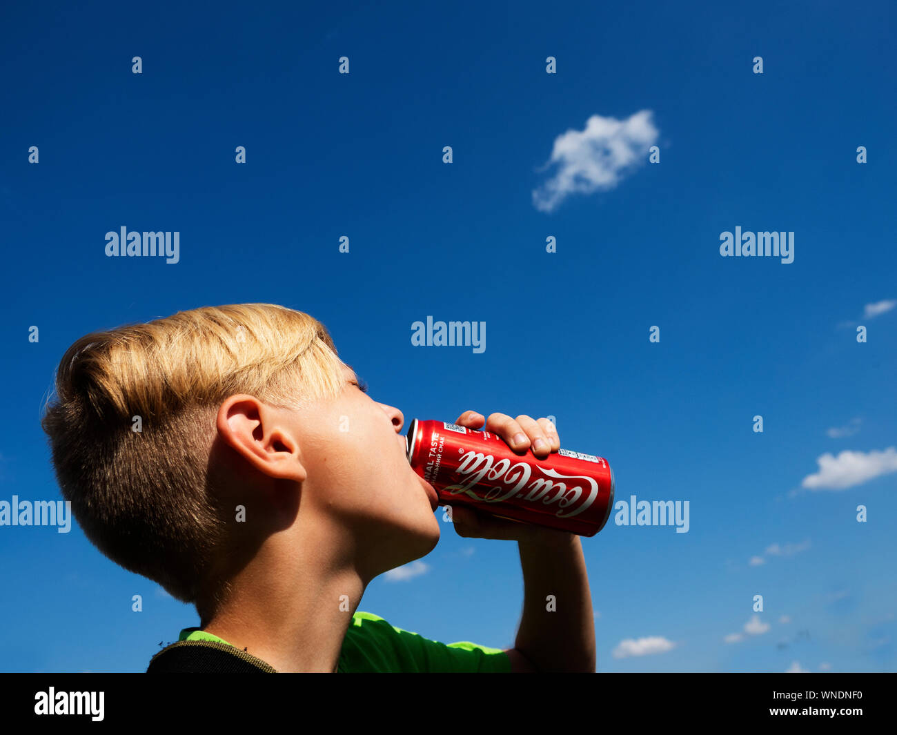 Caucasian blond boy drinking Coca-Cola from the can against blue sky ...