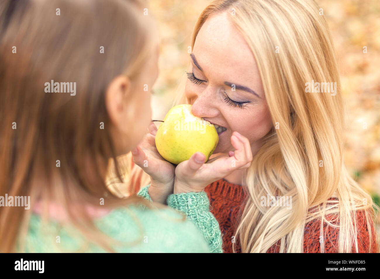 Mother and daughter eating an apple in the autumn park. Mother and her ...