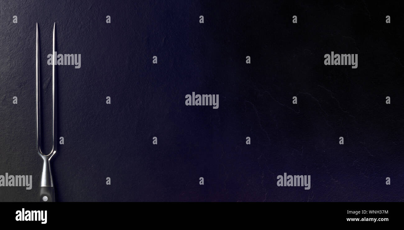 Meat carving fork on black, a panorama with a place for text, abstract ...