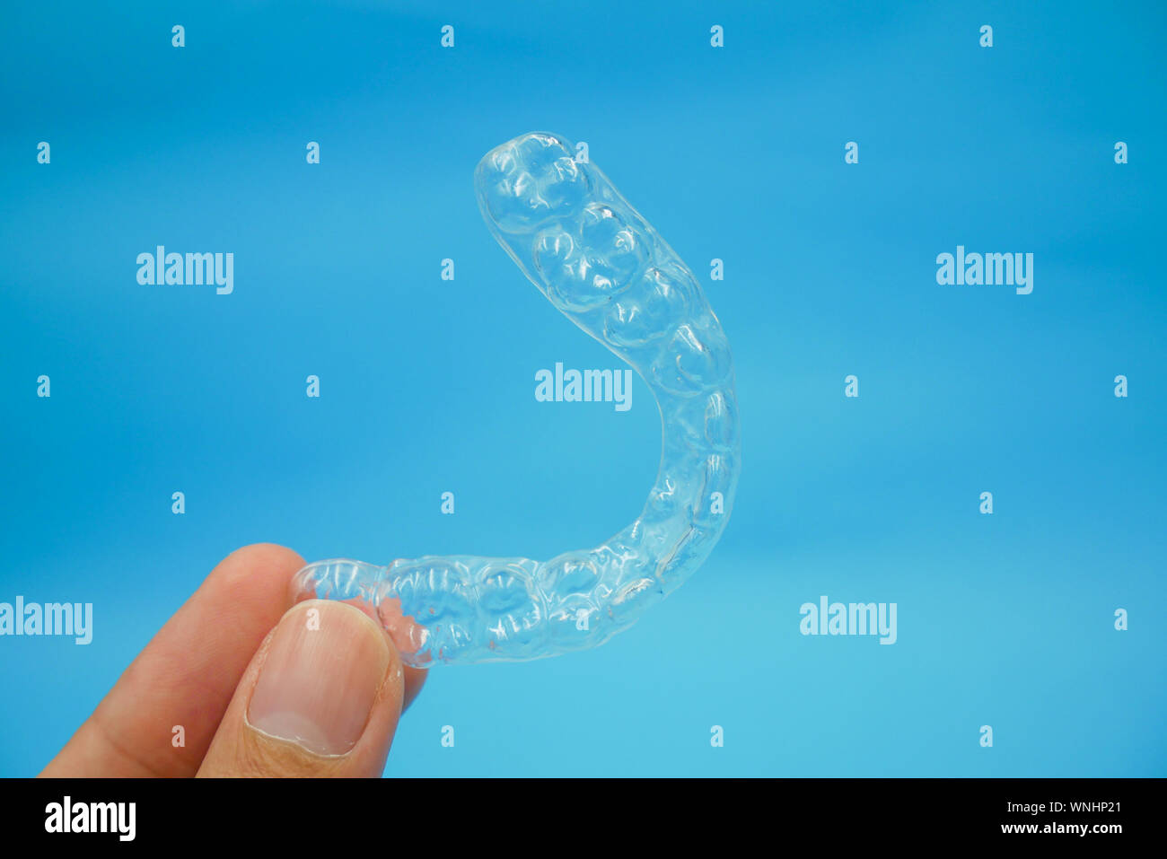 hand holding clear plastic retainer teeth that isolated on blue sky ...