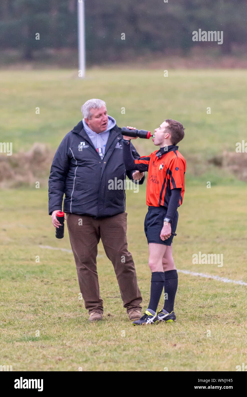 Young rugby referee takes a drink from water bottle as larger coach ...