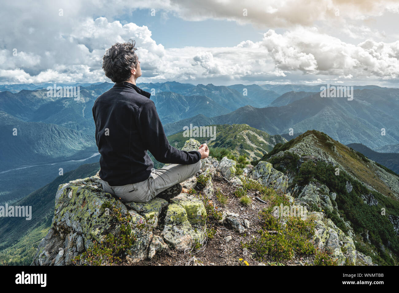 Man hiker sitting in a yoga pose at the peak of the mountain in the ...