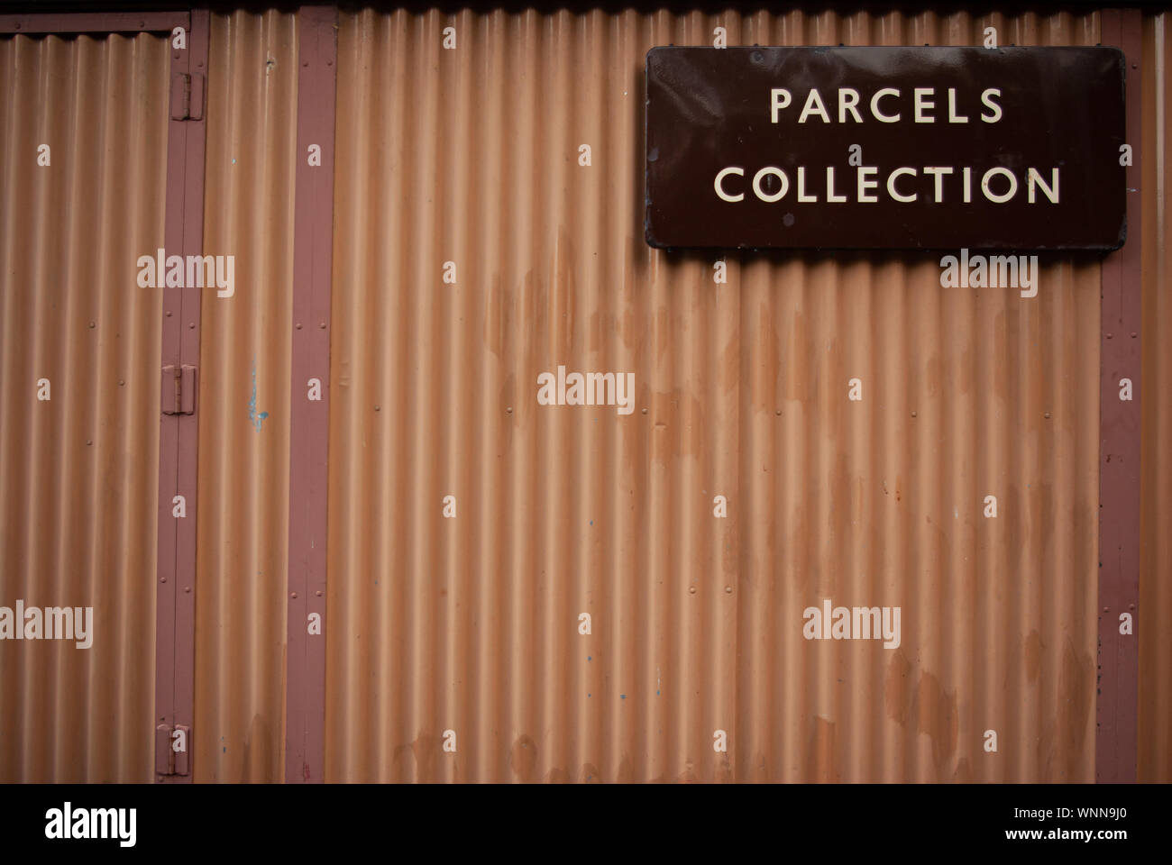 Corrugated brown wall with 'parcels collection' sign Stock Photo - Alamy