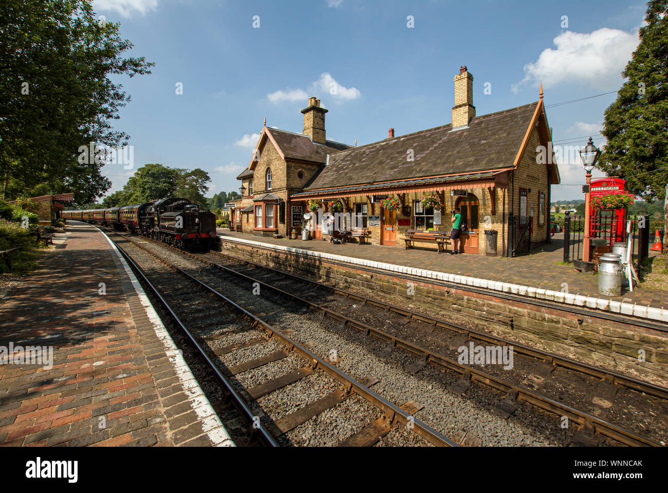 Steam train arrives at railway station platform with passengers waiting ...