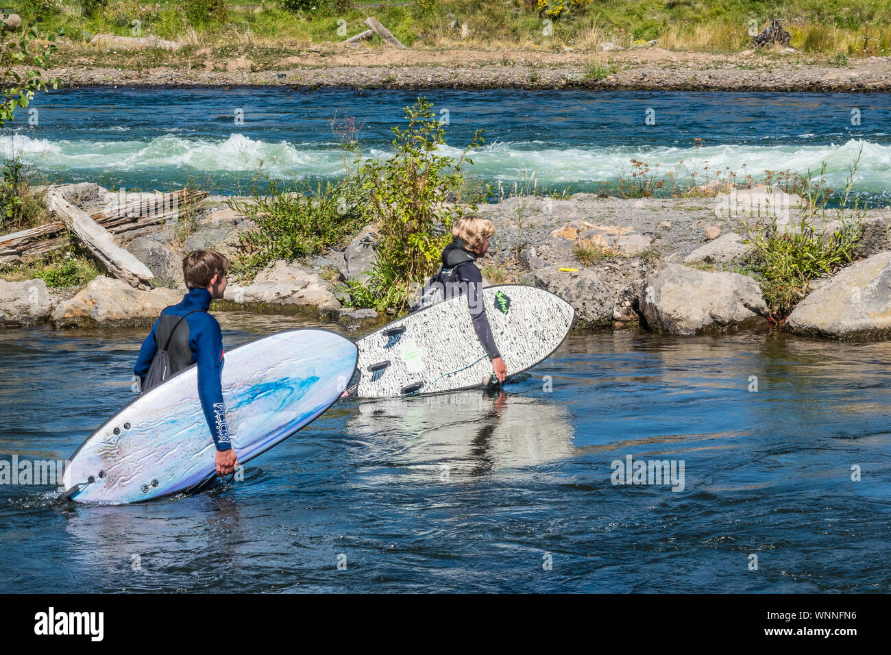 Two teenage river surfers carry their surf boards and cross part of the ...