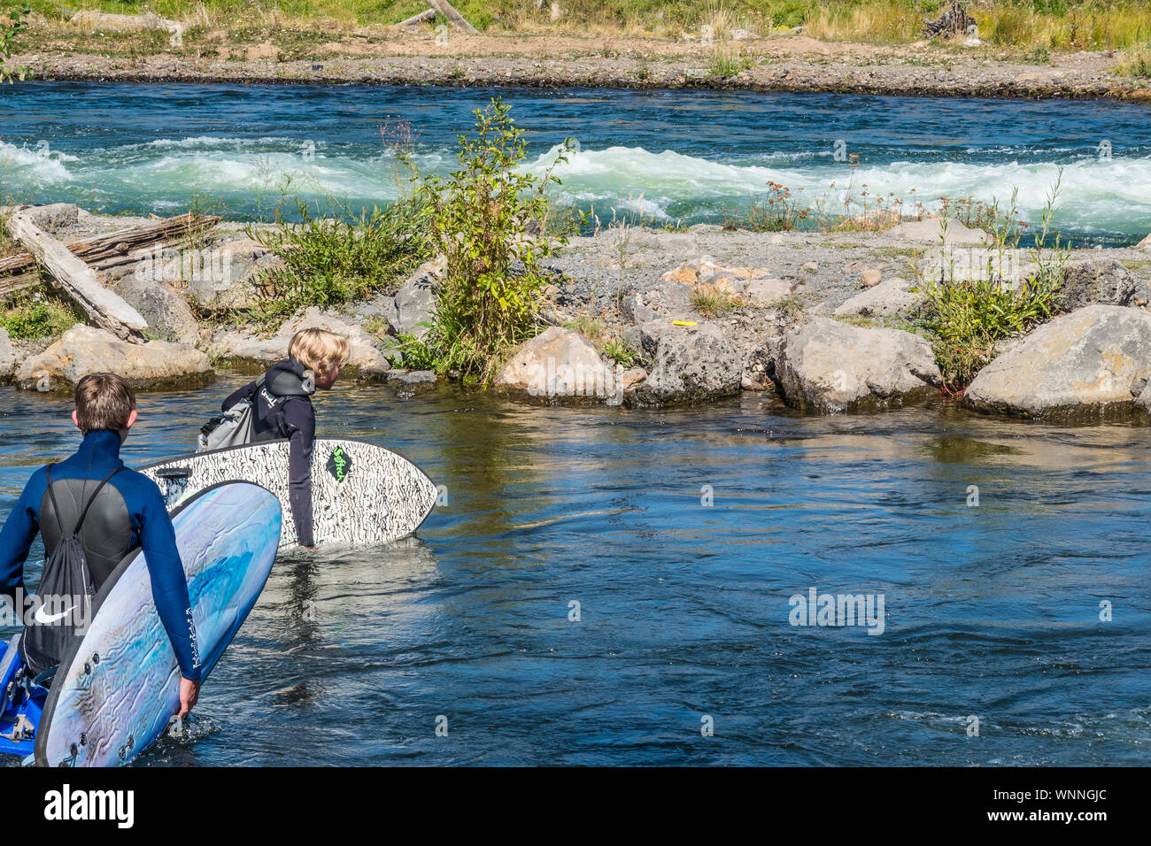 Two teenage river surfers carry their surf boards and cross part of the ...