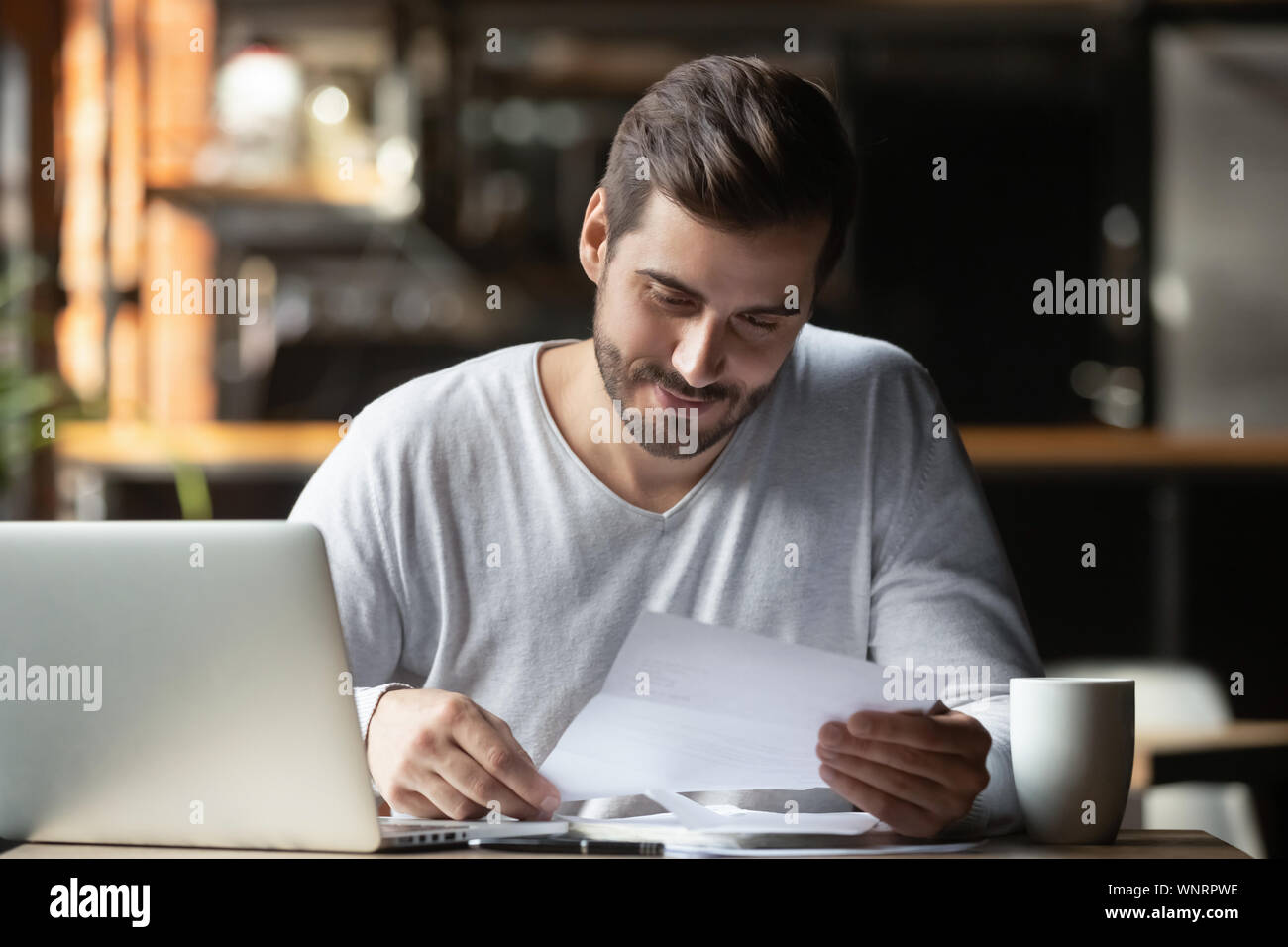 Satisfied man doing paperwork in cafe, holding letter or legal document ...