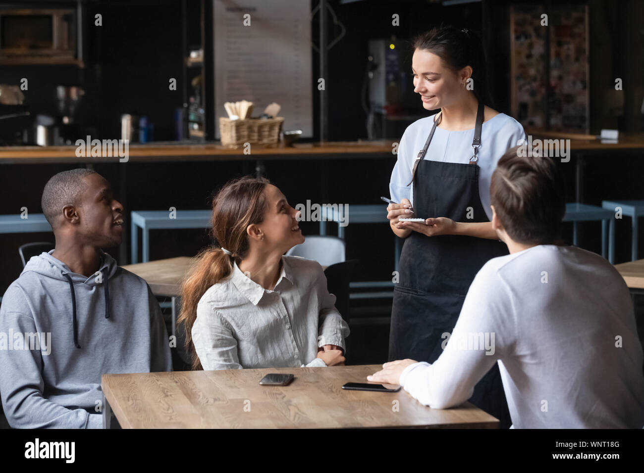 Diverse friends making order in cafe, smiling waitress serving ...