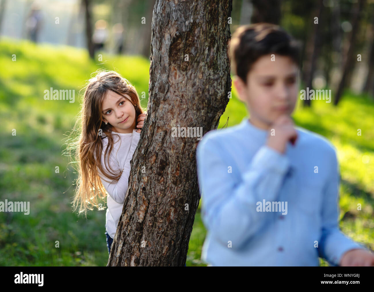 Boy and girl playing hide and seek in the park. Girl watching on ...
