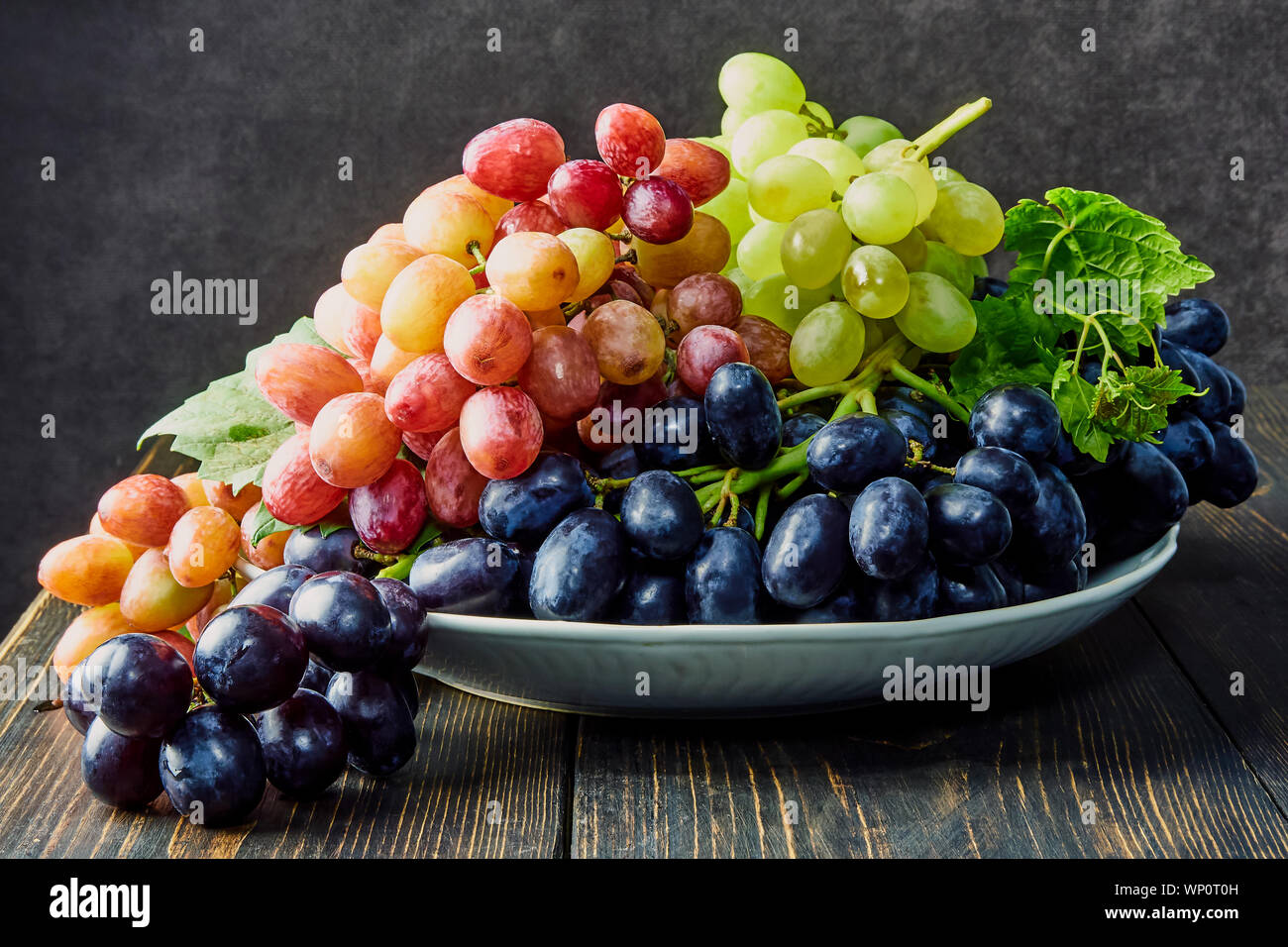 Fresh grapes. Bunches of different varieties in a plate on an old ...