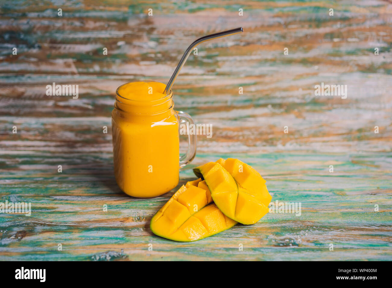 Mango smoothie and steel drinking straw on a painted wooden background ...